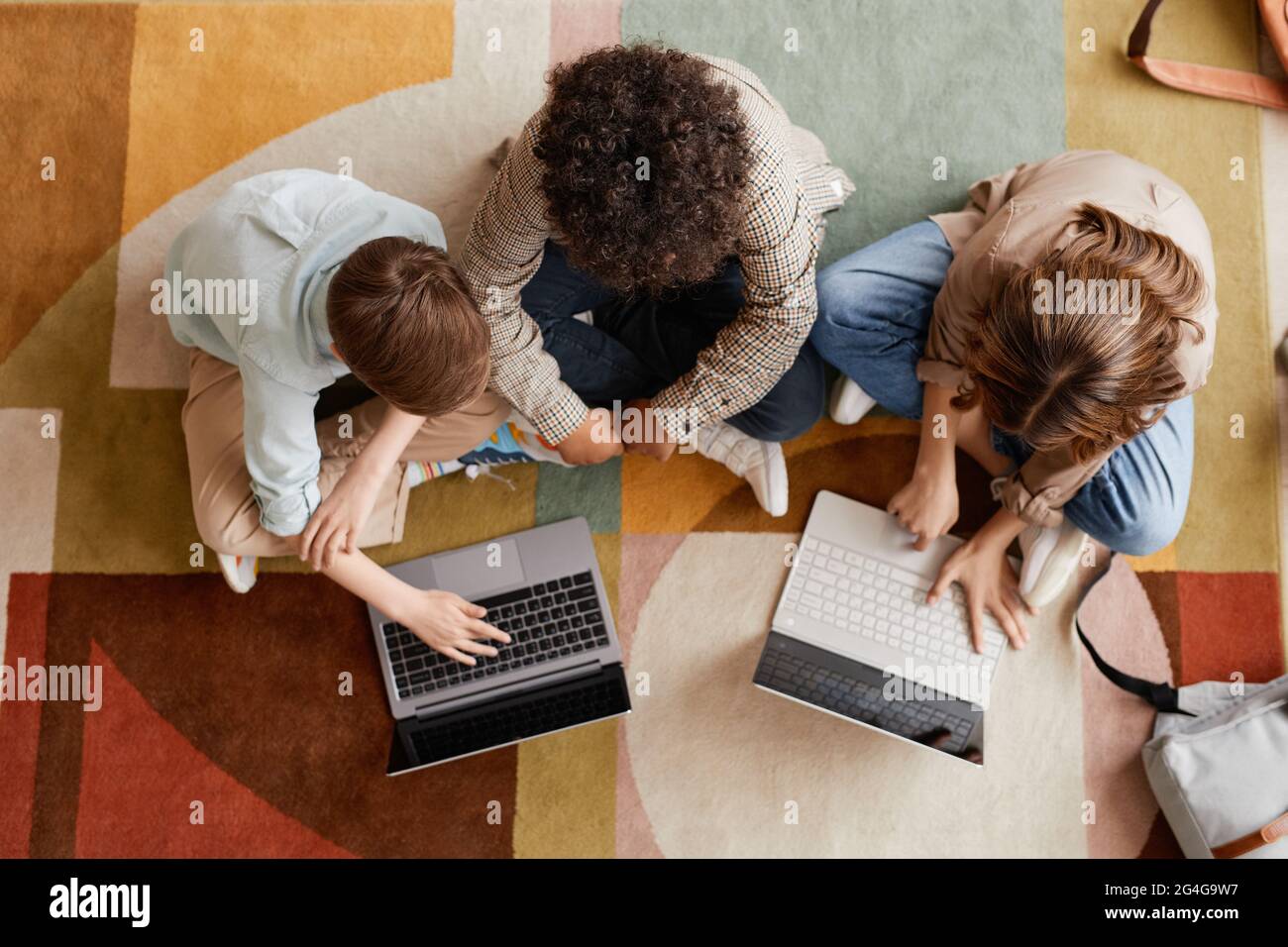 Top down view at group of three kids using computers while sitting on ...