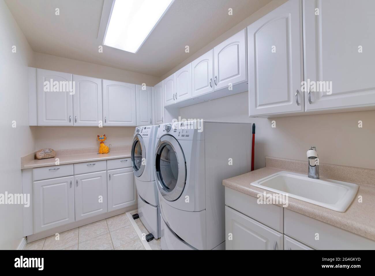 A modern laundry room with white wooden shelves, sink and two washing ...