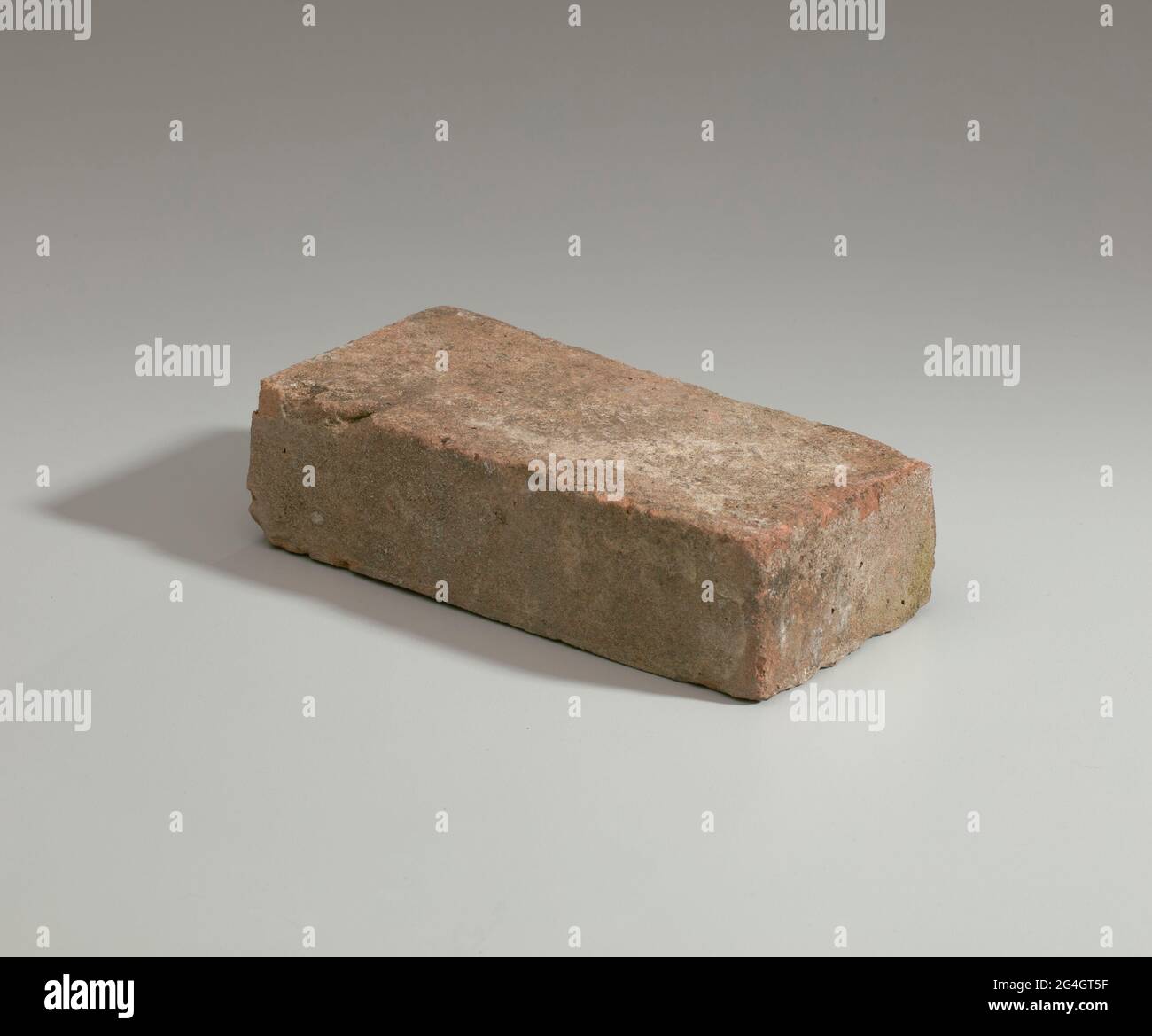 A solid clay brick, a medium beige in color, with uneven edges and ...