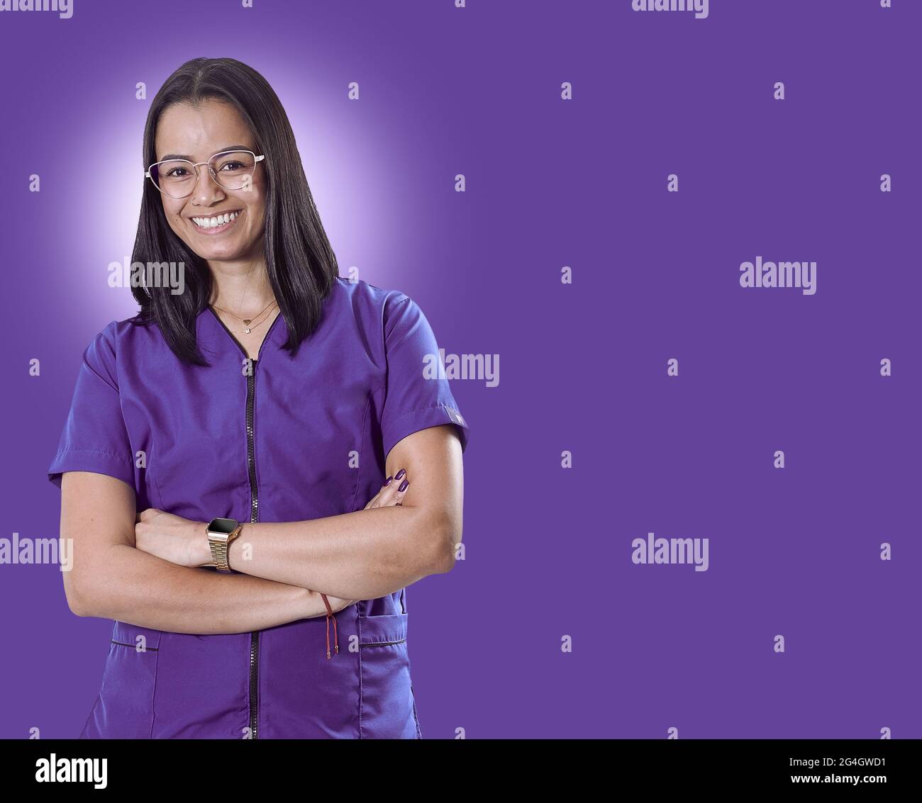 Cheerful young Latina doctor/nurse standing hands crossed on a purple ...