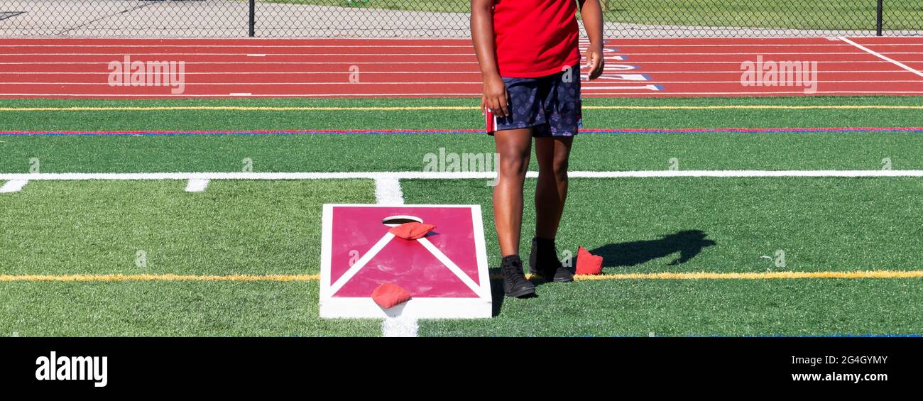 A cornhole player standing next to a homemade board playing cornhole on ...
