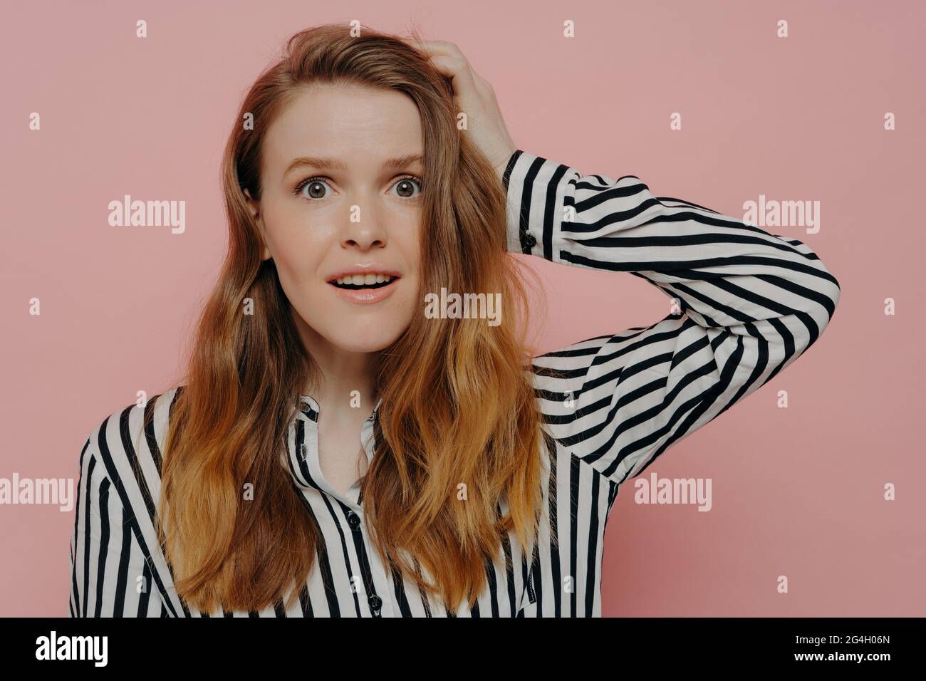 Shocked young woman with ginger hair looking at camera touching head ...