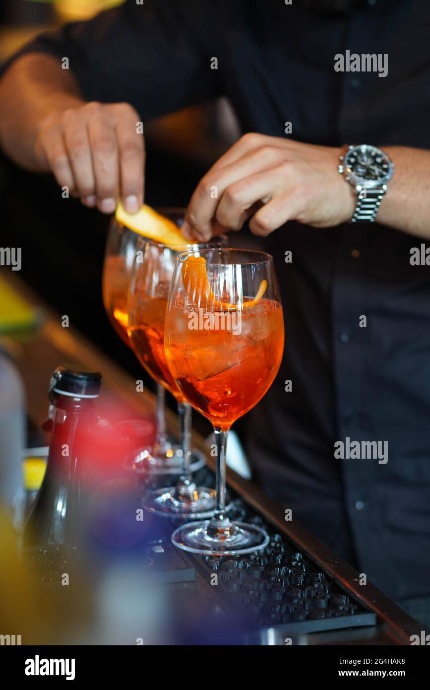 three glasses of cocktails on the bar. bartender pours a glass of sparkling wine with Aperol ...