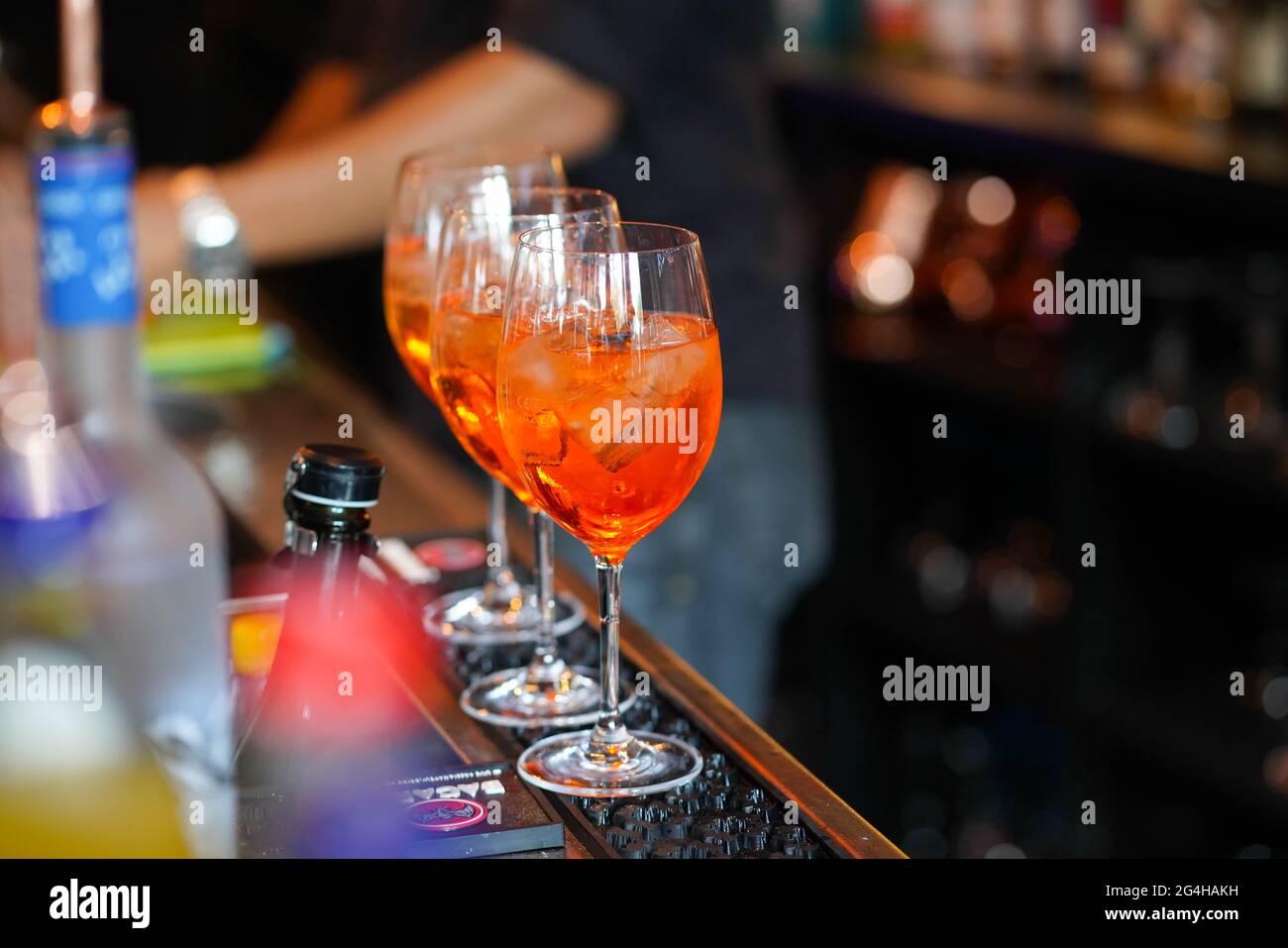 three glasses of cocktails on the bar. bartender pours a glass of sparkling wine with Aperol ...