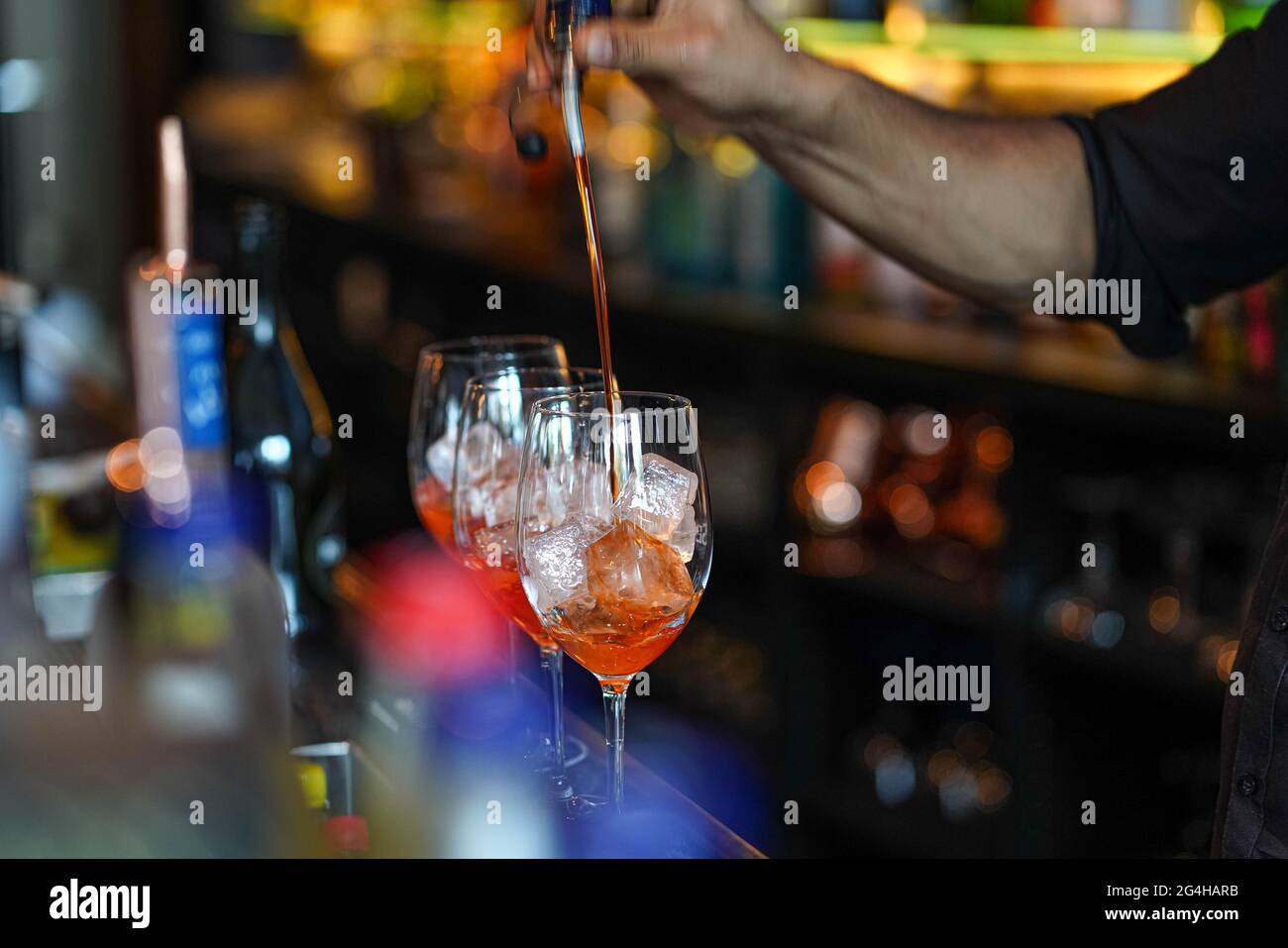 three glasses of cocktails on the bar. bartender pours a glass of sparkling wine with Aperol ...