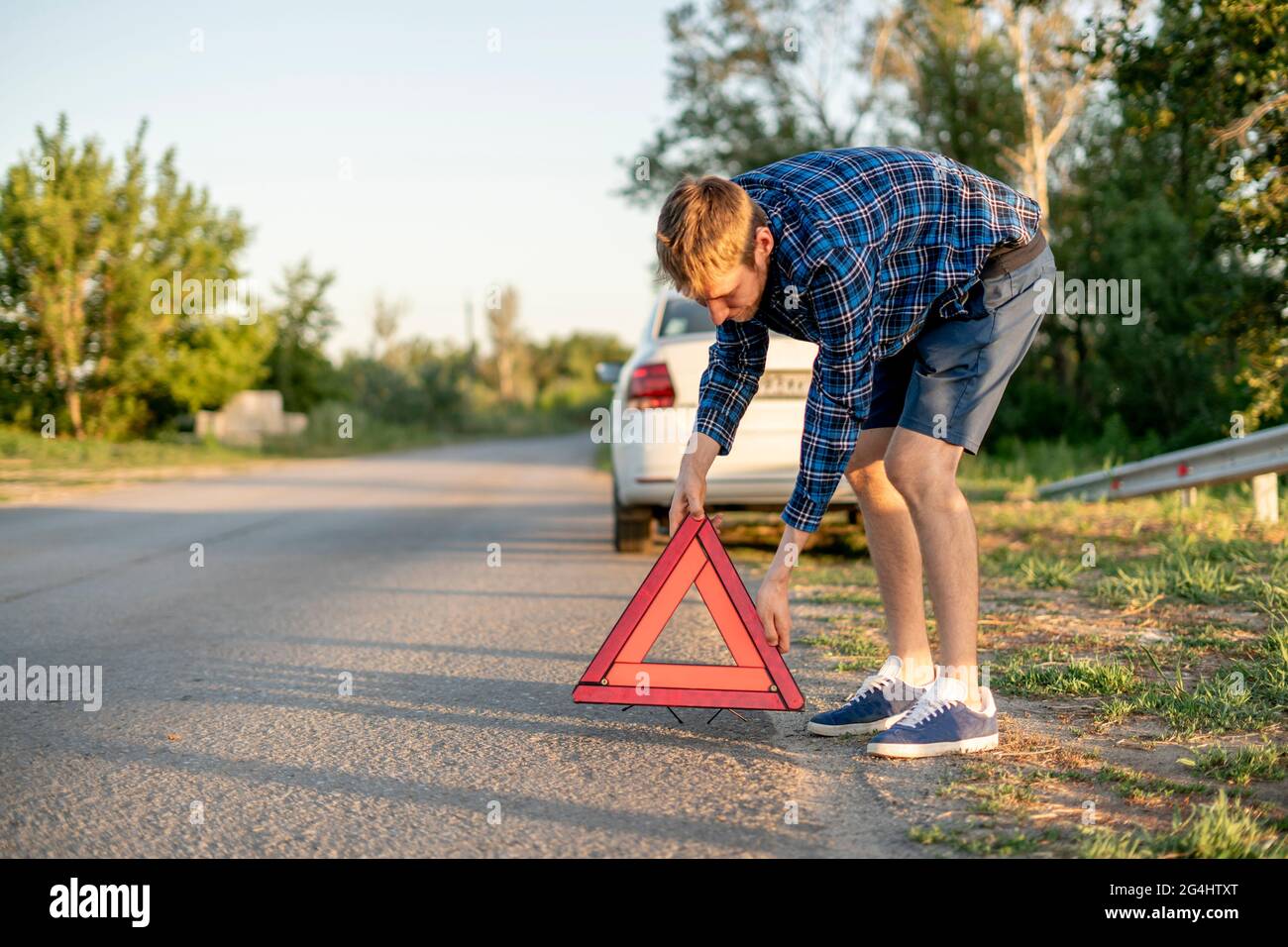 young man holding a red triangle and put it on the road, the sign of ...