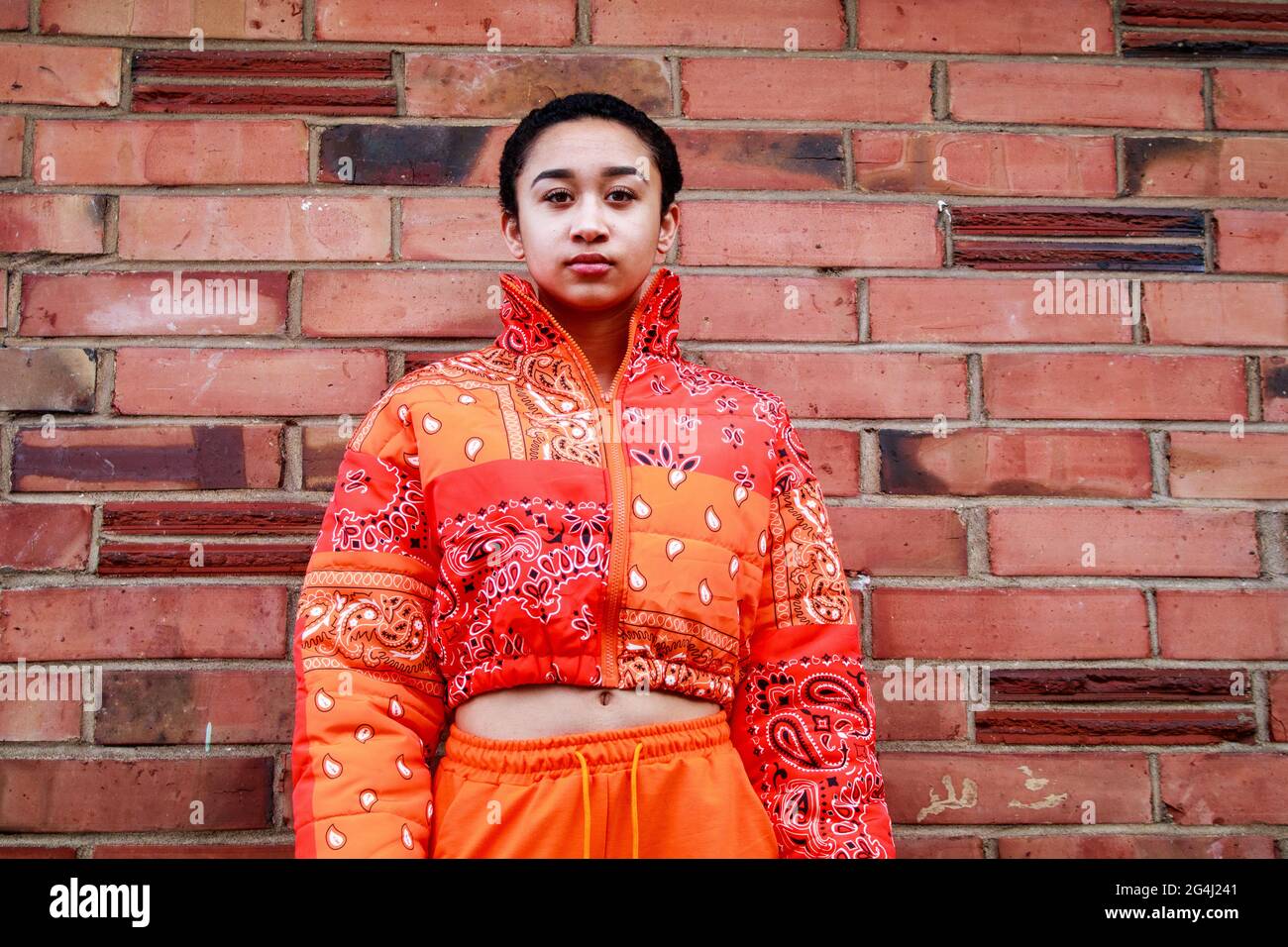 Titled: Power - Girl standing in front of brick wall, wearing an orange ...