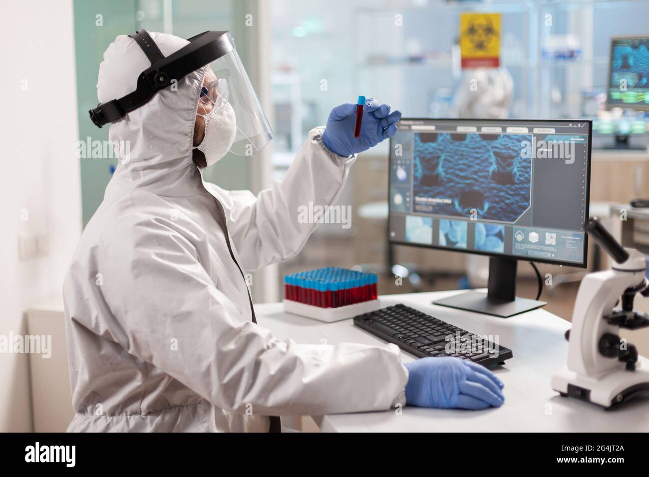 Doctor conducting experiment in lab holding vaccutainer dressed in ppe ...