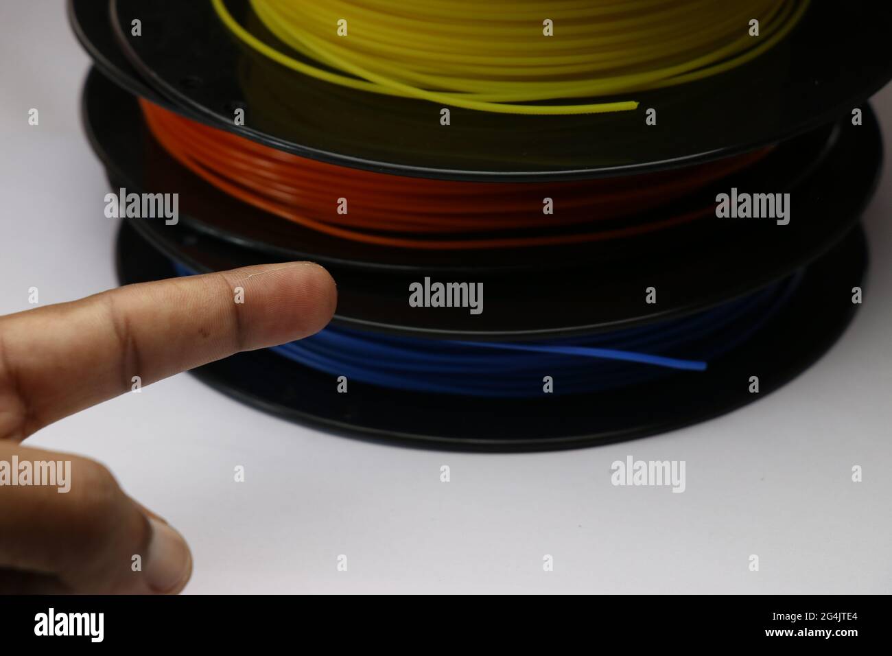 Hand pointing towards 3D printer filaments laid flat on spools with ...