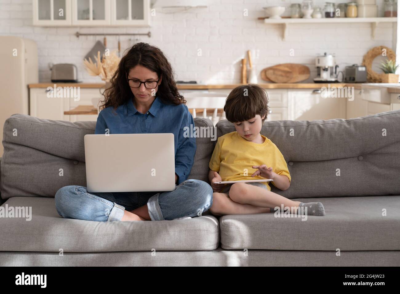 Concentrated mother, son use laptop and tablet computers sit on couch ...