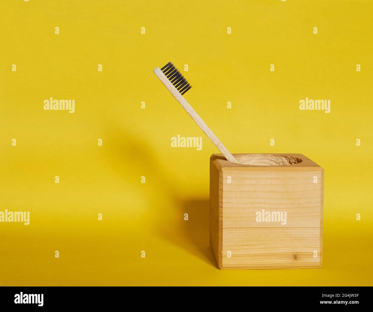 Wooden toothbrush in a wooden stand on a yellow background. Horizontal ...