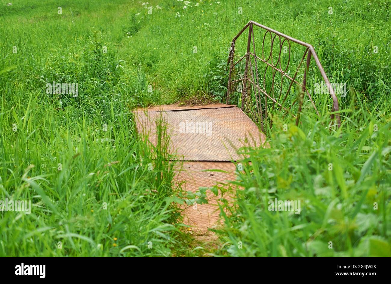 A rusty metal pedestrian bridge spanning a grassy stream Stock Photo ...
