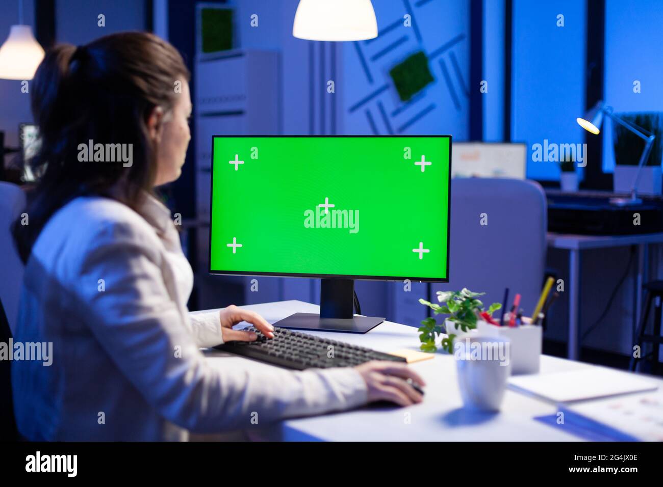 Businesswoman looking at green screen monitor of computer sitting at ...
