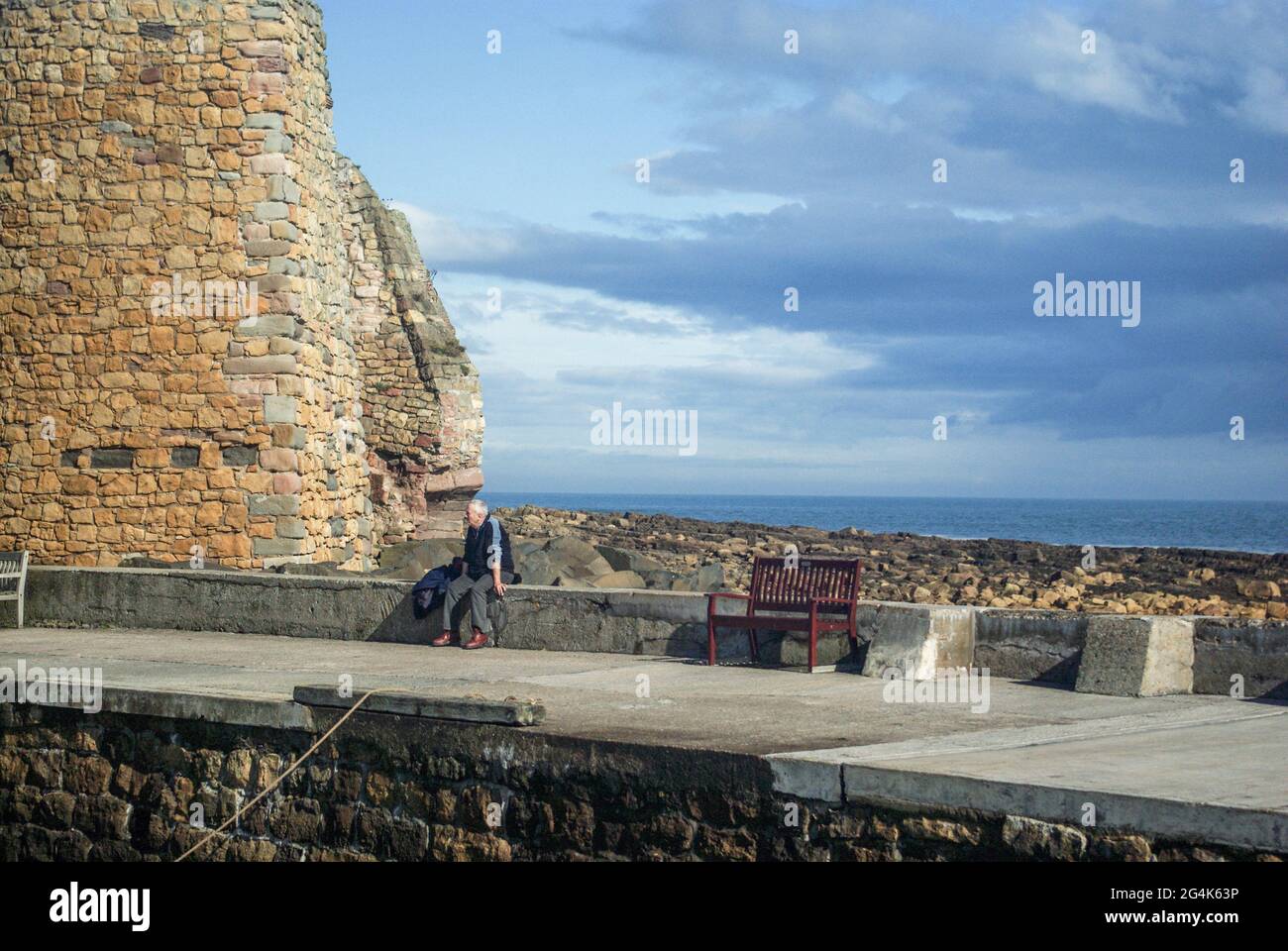 Beadnell Harbour, Beadnell, Northumberland, UK; visitor sitting on the ...