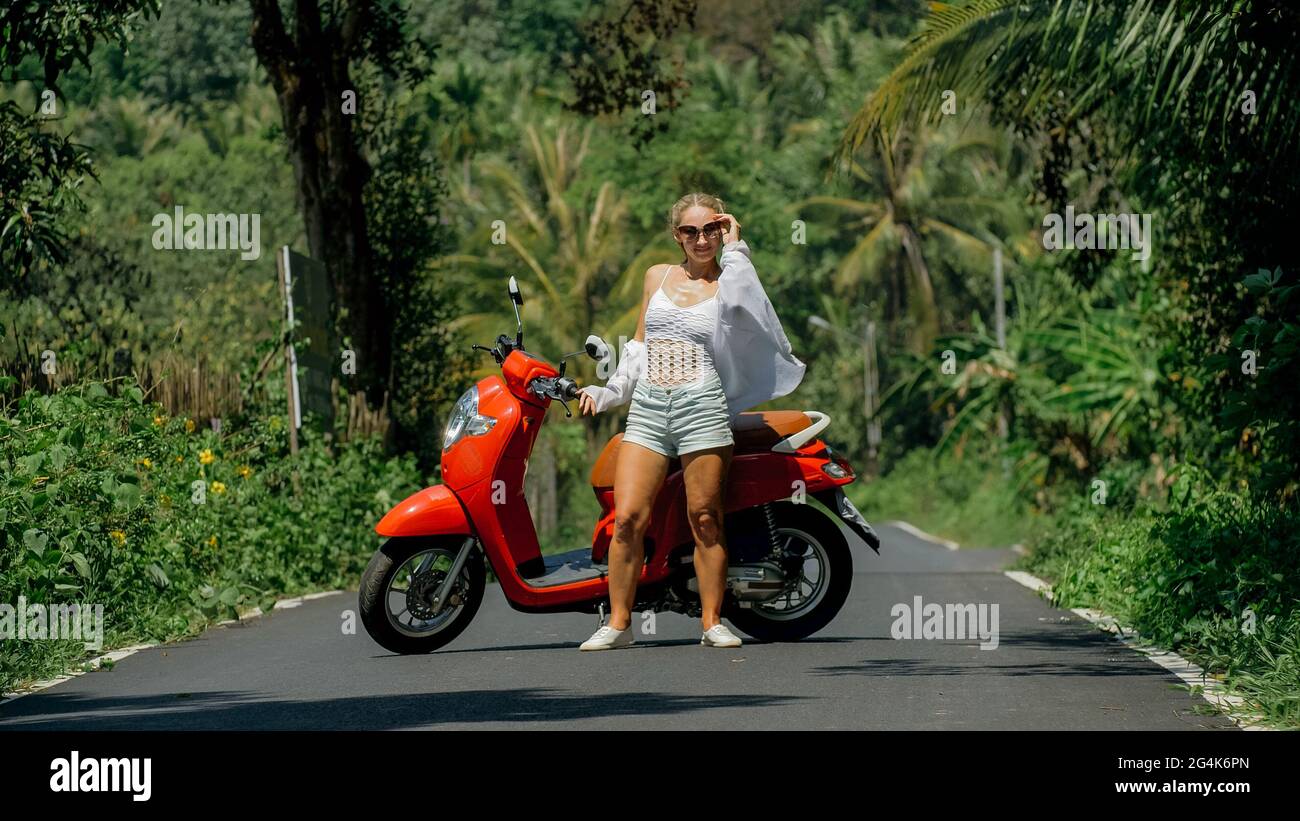 Woman on red scooter in white clothes drive on forest road trail ...
