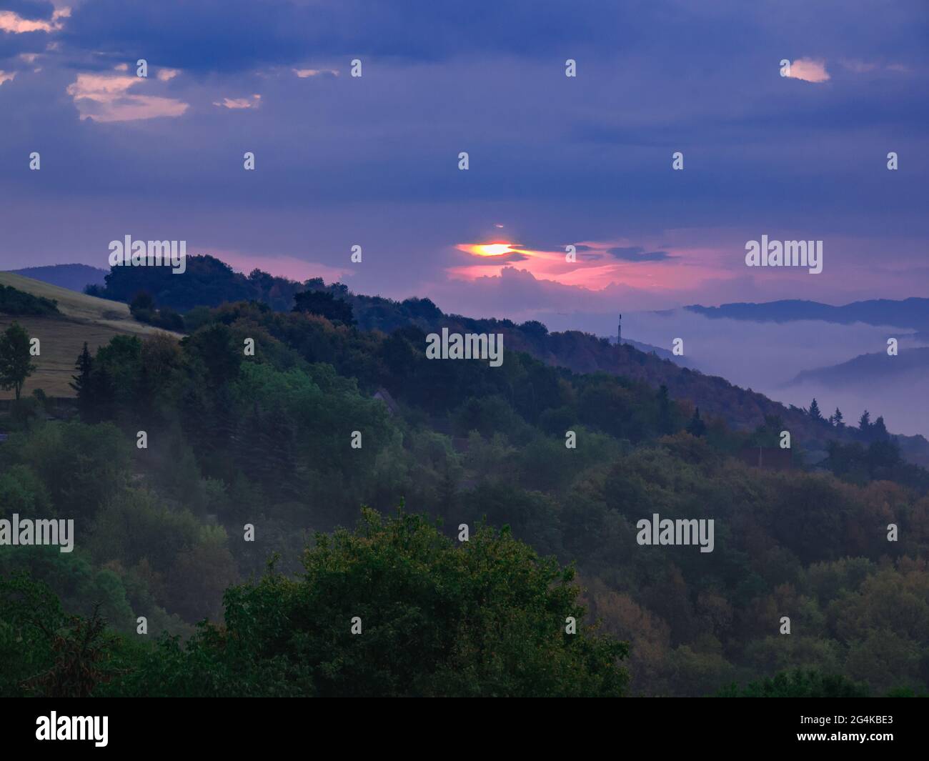 Early morning sun peeks from behind heavy rain clouds with a dense fog ...