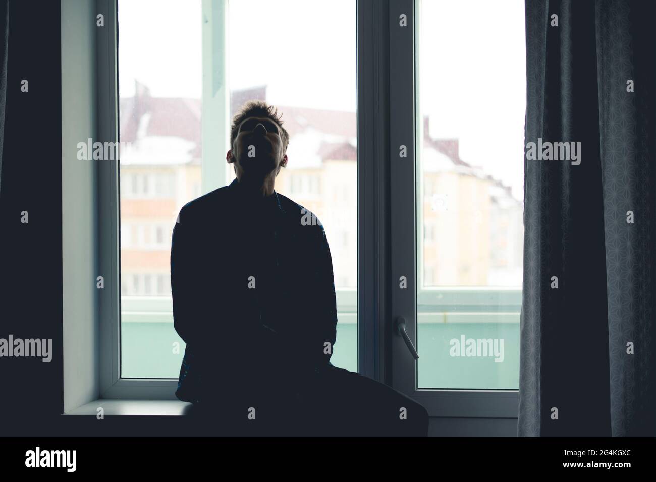sad lonely thoughtful man silhouette sitting on a window windowsill and ...