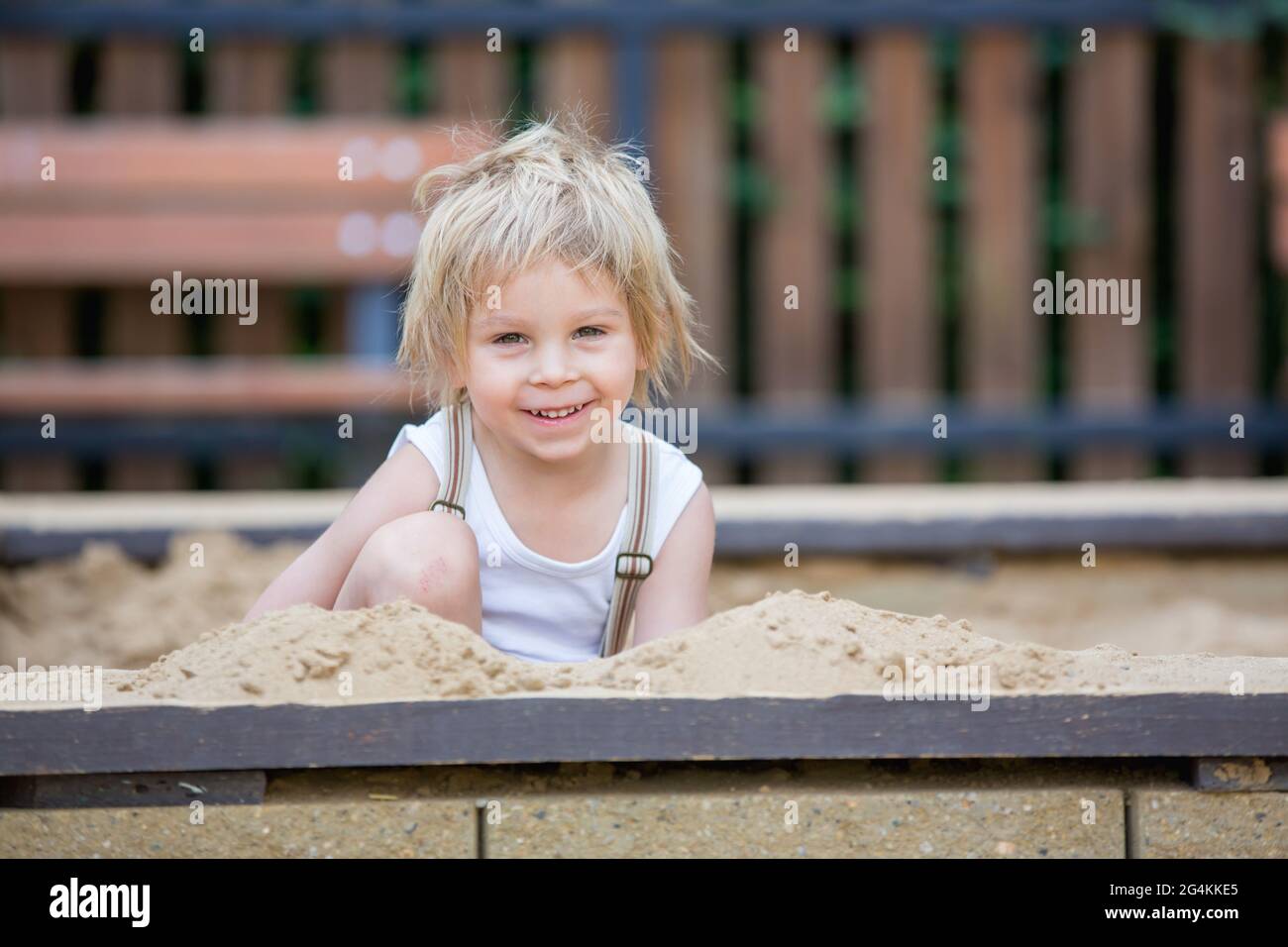 Cute toddler child, blond boy, playing in the sandpit in the park ...