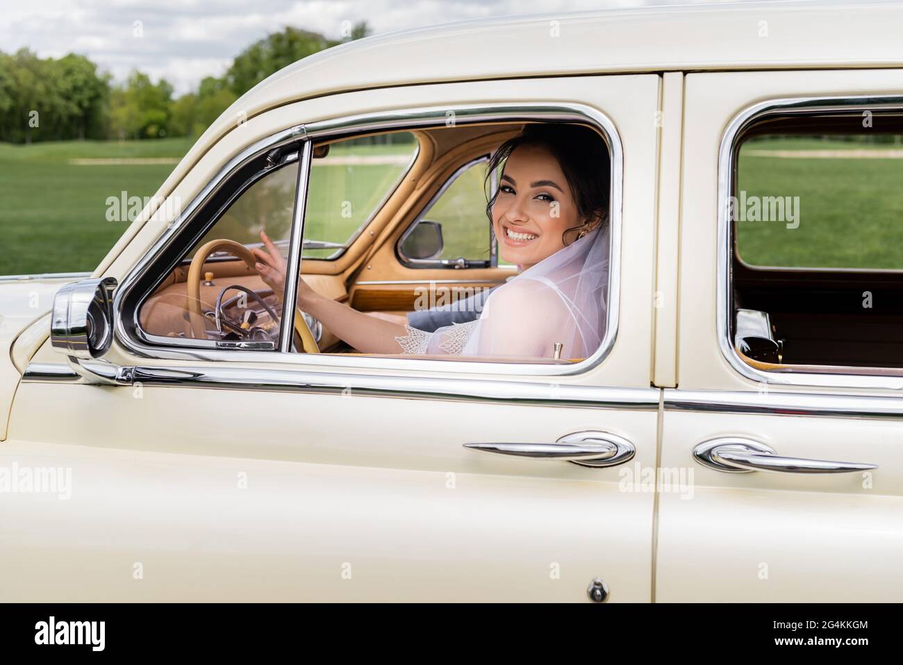 Bride in veil smiling at camera on driver seat of retro car Stock Photo ...