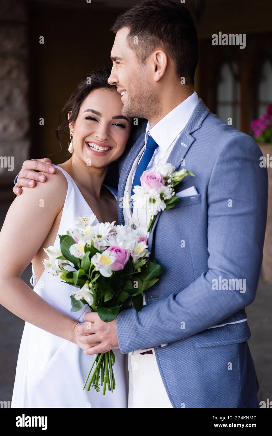 Happy groom hugging bride with bouquet outdoors Stock Photo - Alamy