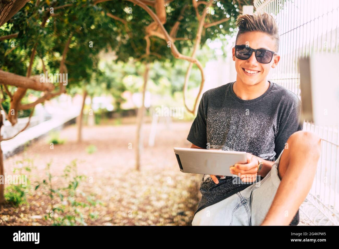 Young boy teenager age use tablet device outdoor in the park smiling ...
