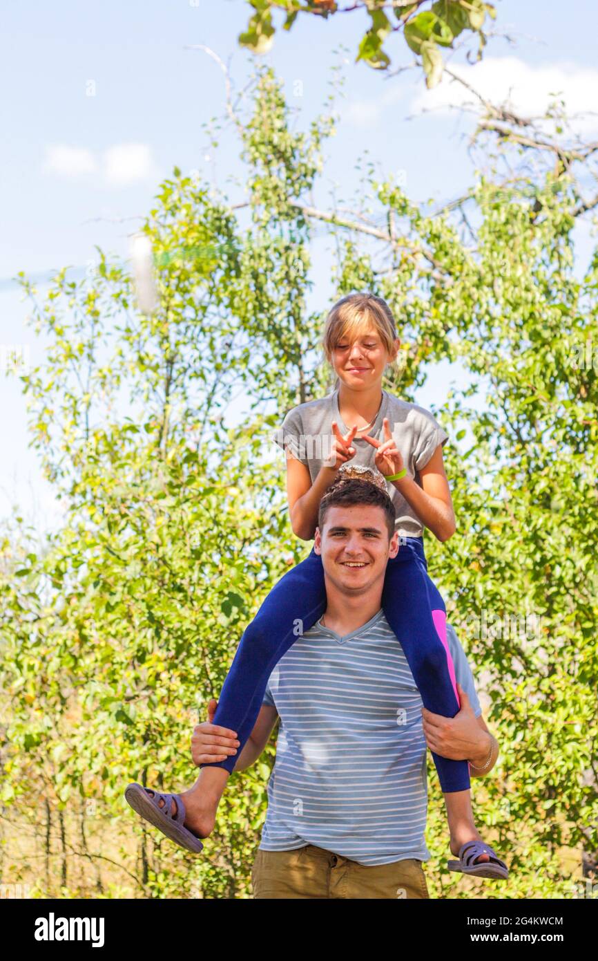 Defocused brother giving sister ride on back. Portrait of happy girl on ...
