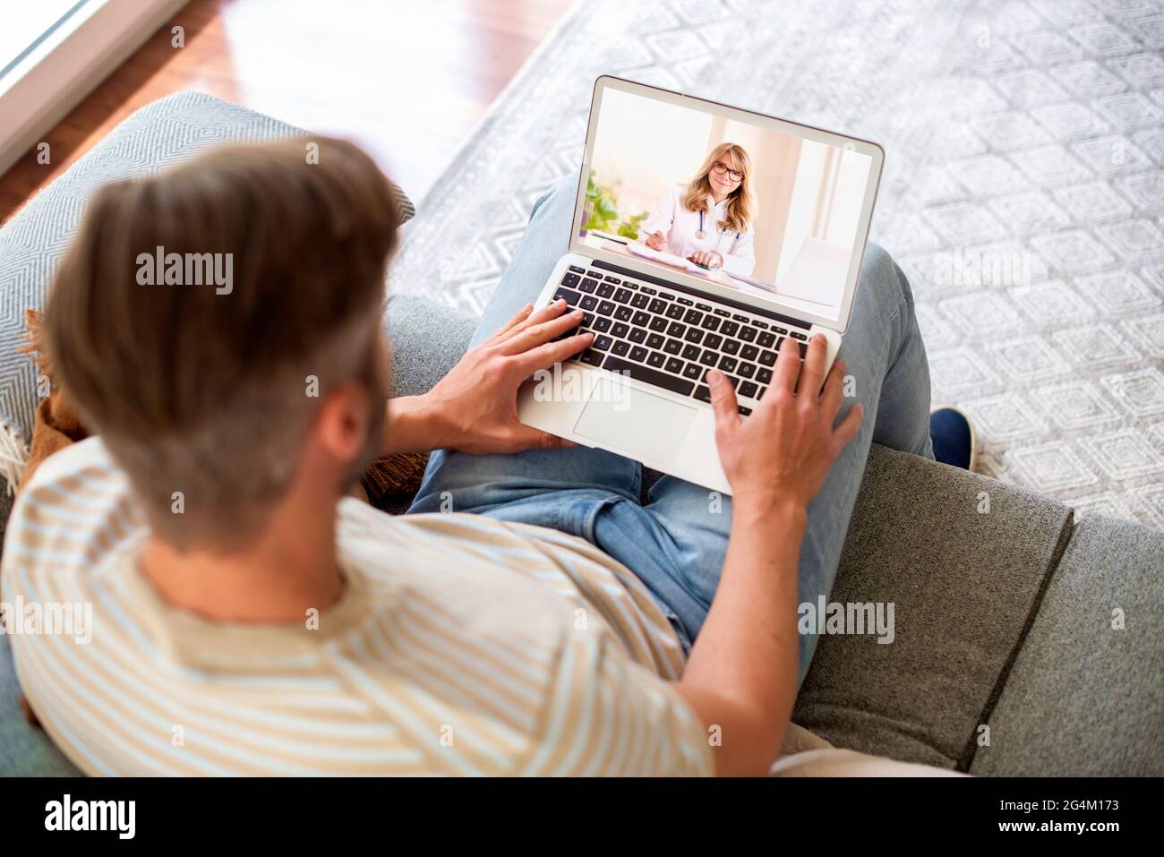 Rear view shot of a man sitting on the couch at home and making a video ...