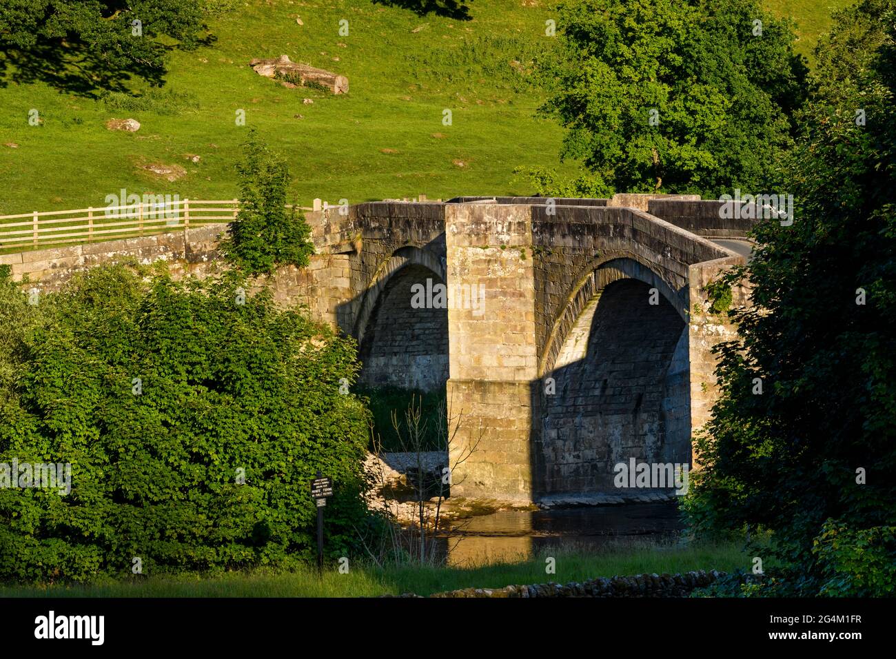 Scenic, sunny riverside view of historic C17 stone arched road bridge ...