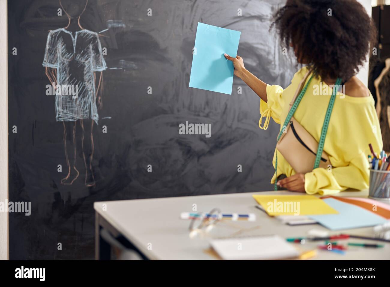 African-American teacher shows blank blue paper against blackboard at ...