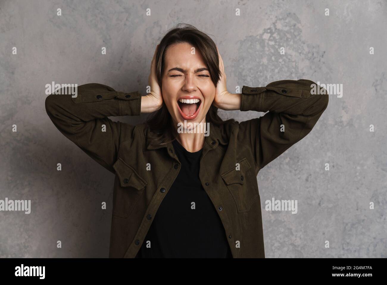 Nervous beautiful girl screaming and covering her ears isolated over ...