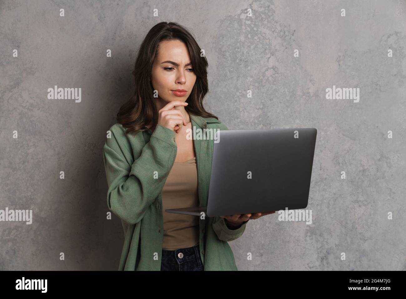 Puzzled beautiful brunette girl thinking and using laptop isolated over ...