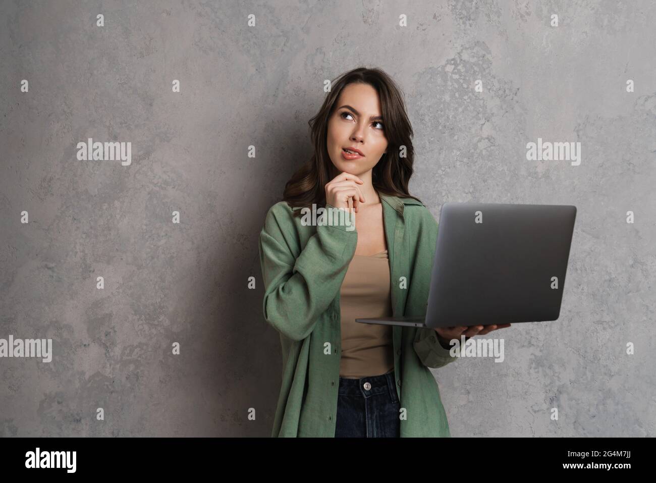 Puzzled beautiful brunette girl thinking and using laptop isolated over ...