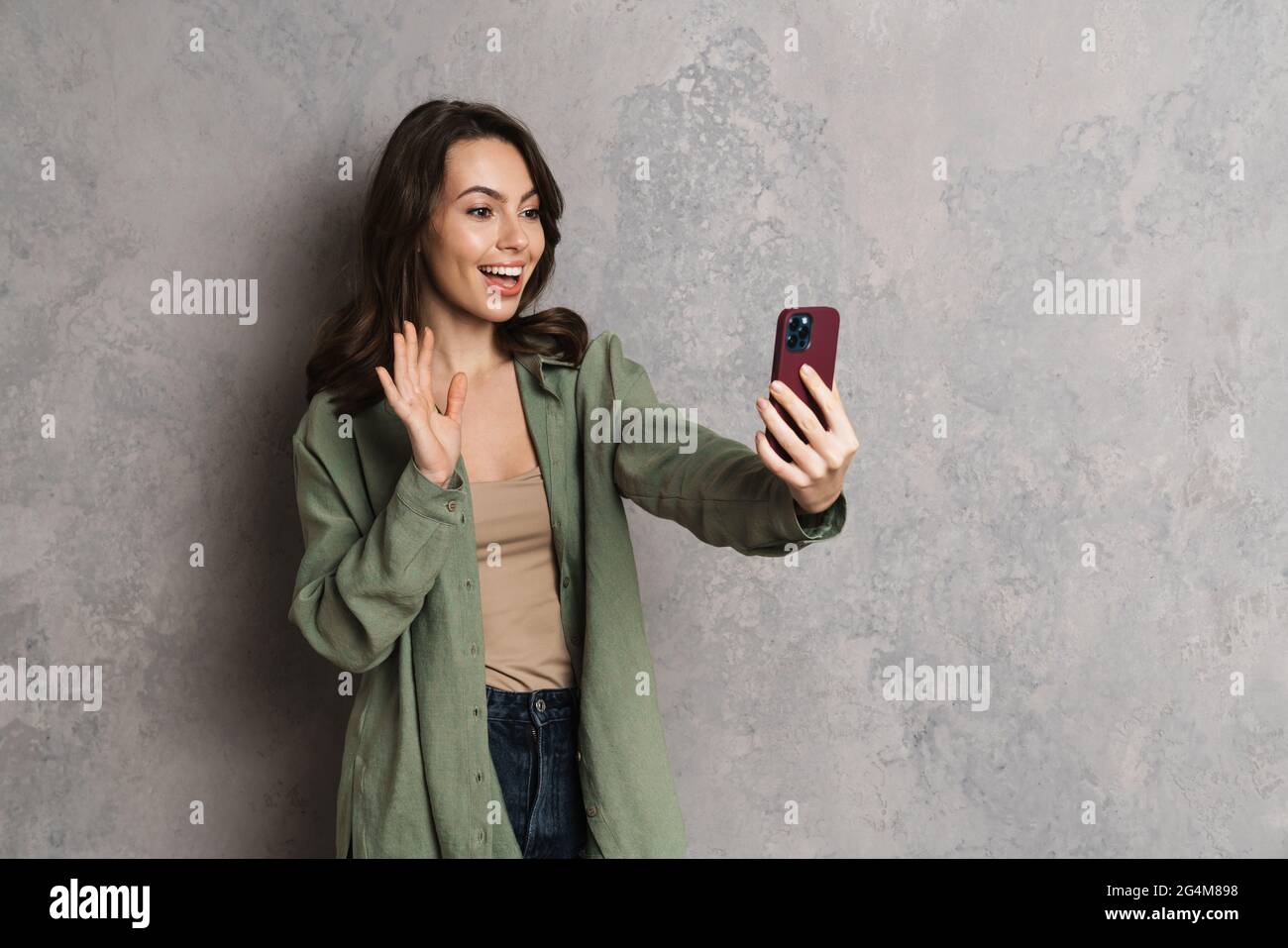 Happy nice girl waving hand while taking selfie on mobile phone ...