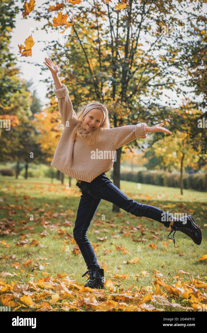 Beautiful little girl jumping with autumn leaves in the park outdoor ...