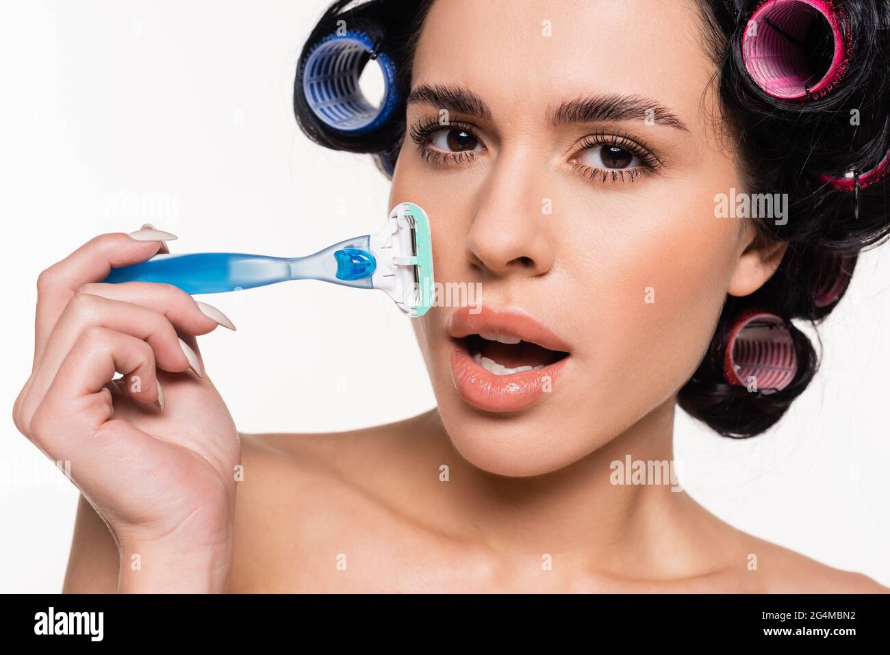 portrait of amazed young woman in curlers holding razor near face with ...