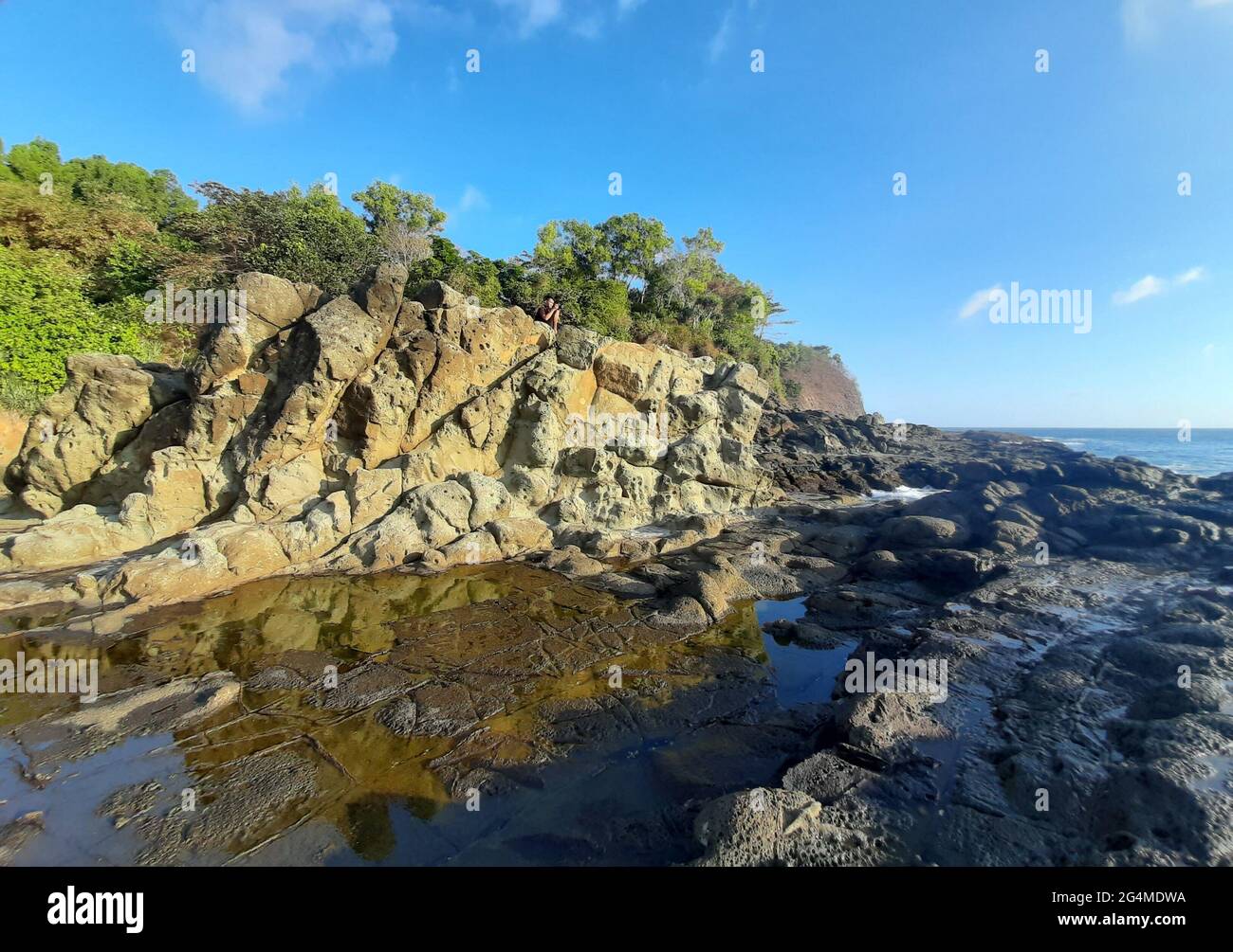 A young Asian photographer sitting on the edge of a rock with rock ...