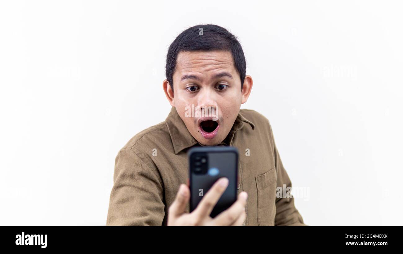 Young Malay man looking at the smartphone screen with a shocked face ...