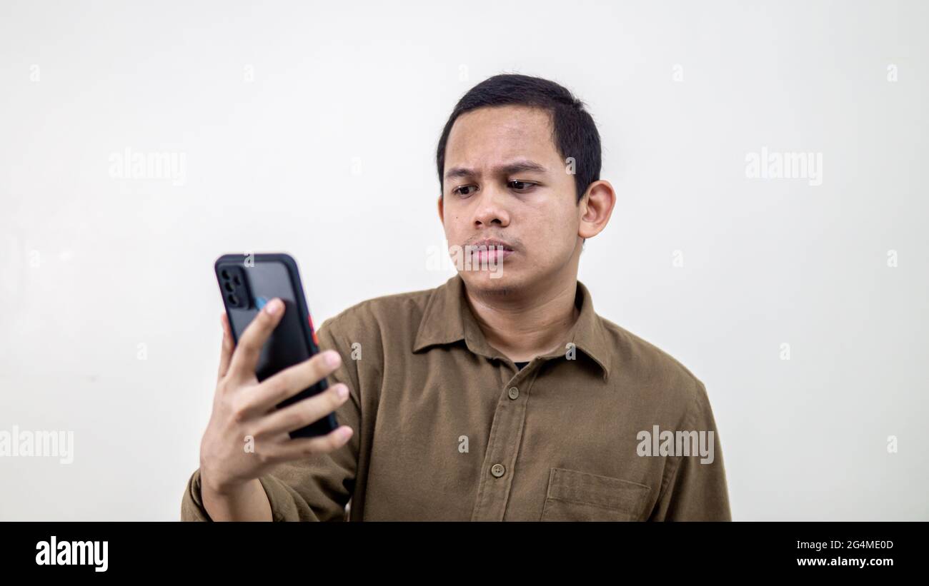 Young Asian Malay Man Looking At The Smartphone With A Serious And