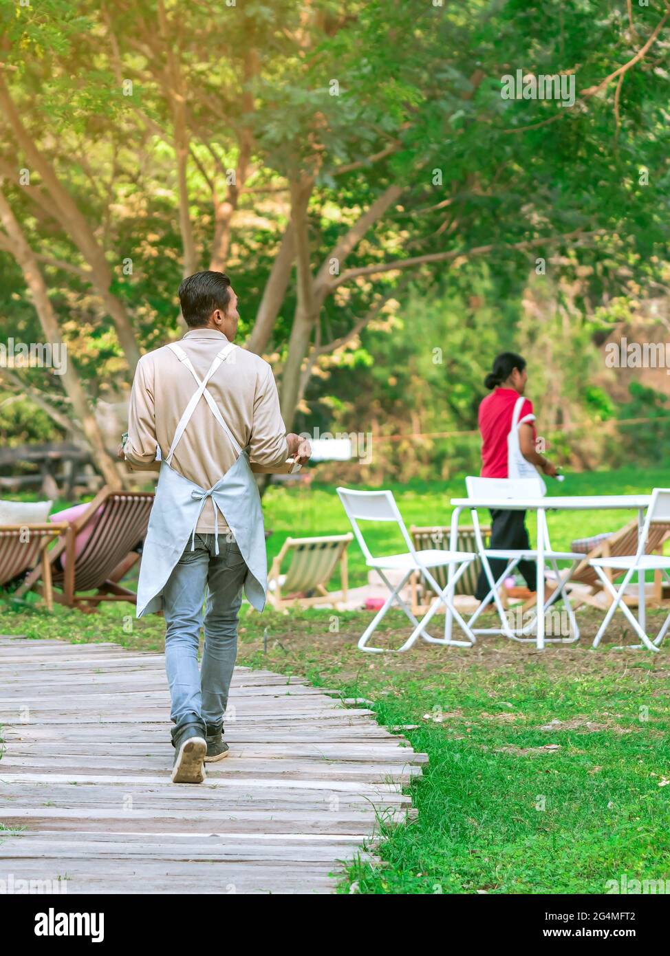 Back view of Asian male waiter carry food and beverages along garden ...