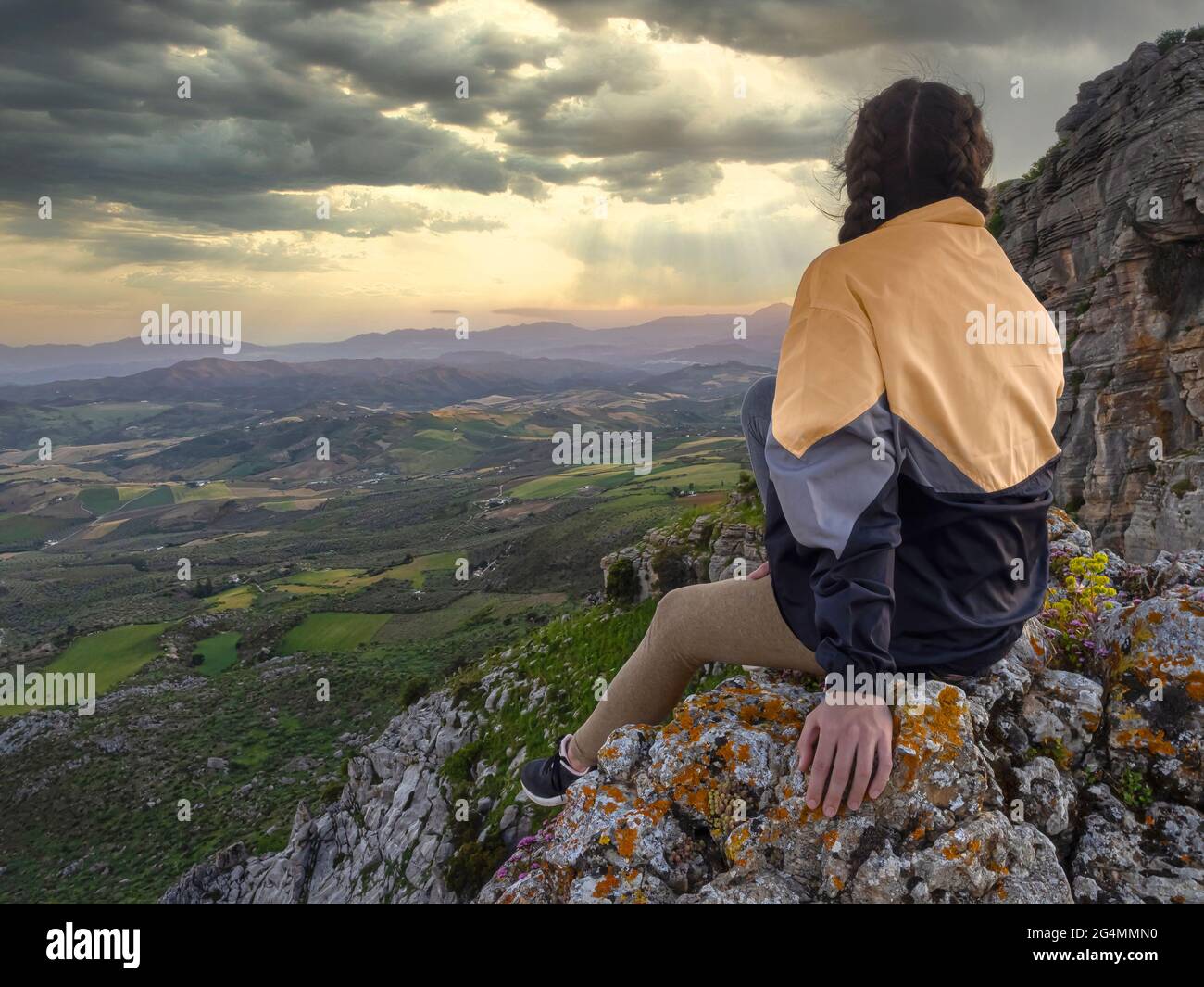 Woman in raincoat standing on the edge of a cliff overlooking a valley ...