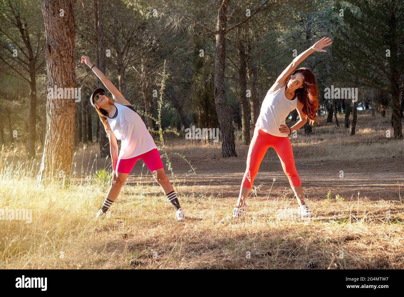 Fitness. Two female runners stretching legs outdoors in park in summer ...