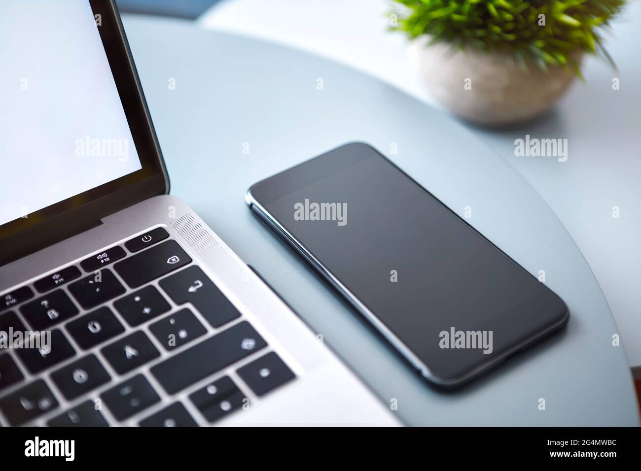 Modern smartphone with rounded edges laying next to laptop on blue ...