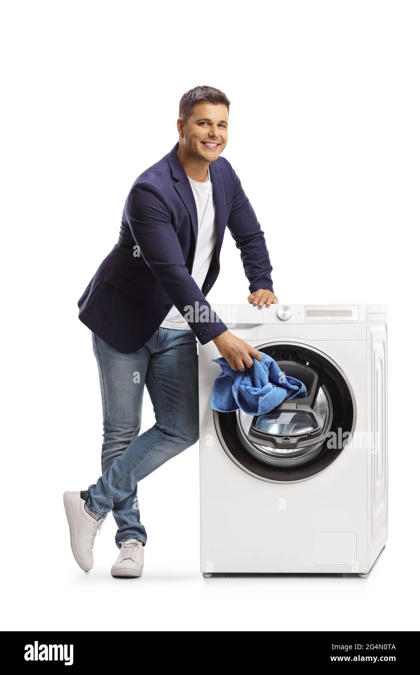 Smiling young man loading a washing machine and looking at camera ...