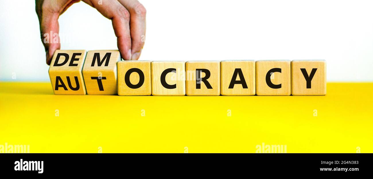 Democracy or autocracy symbol. Businessman turns wooden cubes and ... Democracy or autocracy symbol. Businessman turns wooden cubes and ...