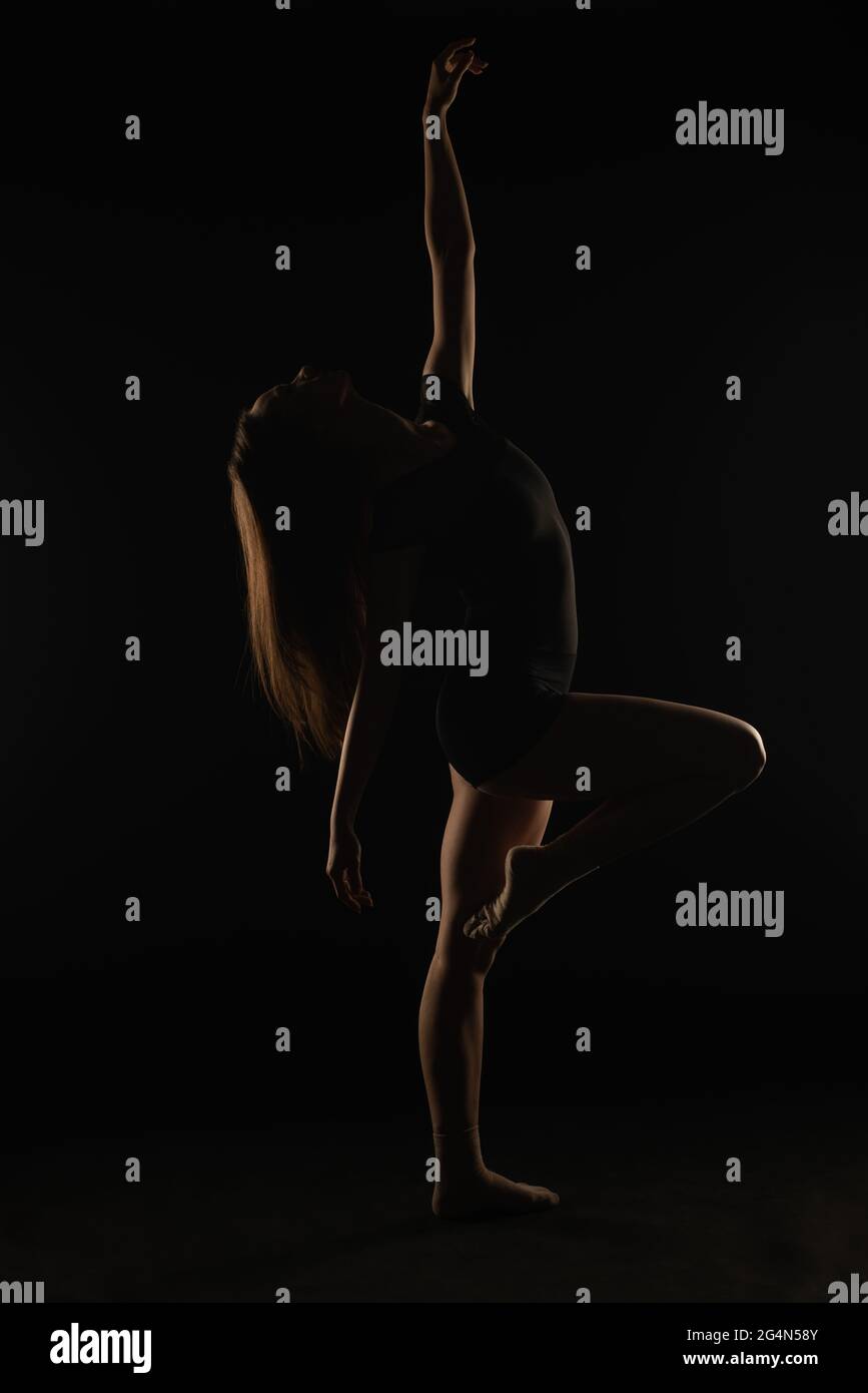 Young ballerina in studio is bending her back while standing on one leg ...