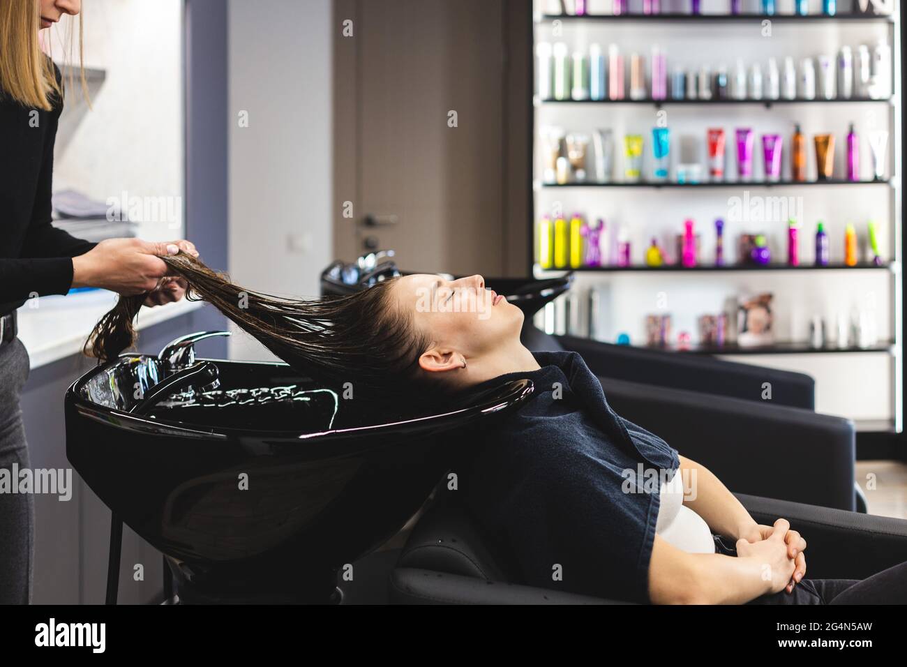 Master woman hairdresser gently washes the girl's hair with shampoo and ...