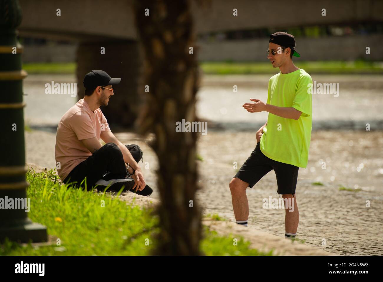 Two male friends are smiling and talking while one of the is sitting on ...