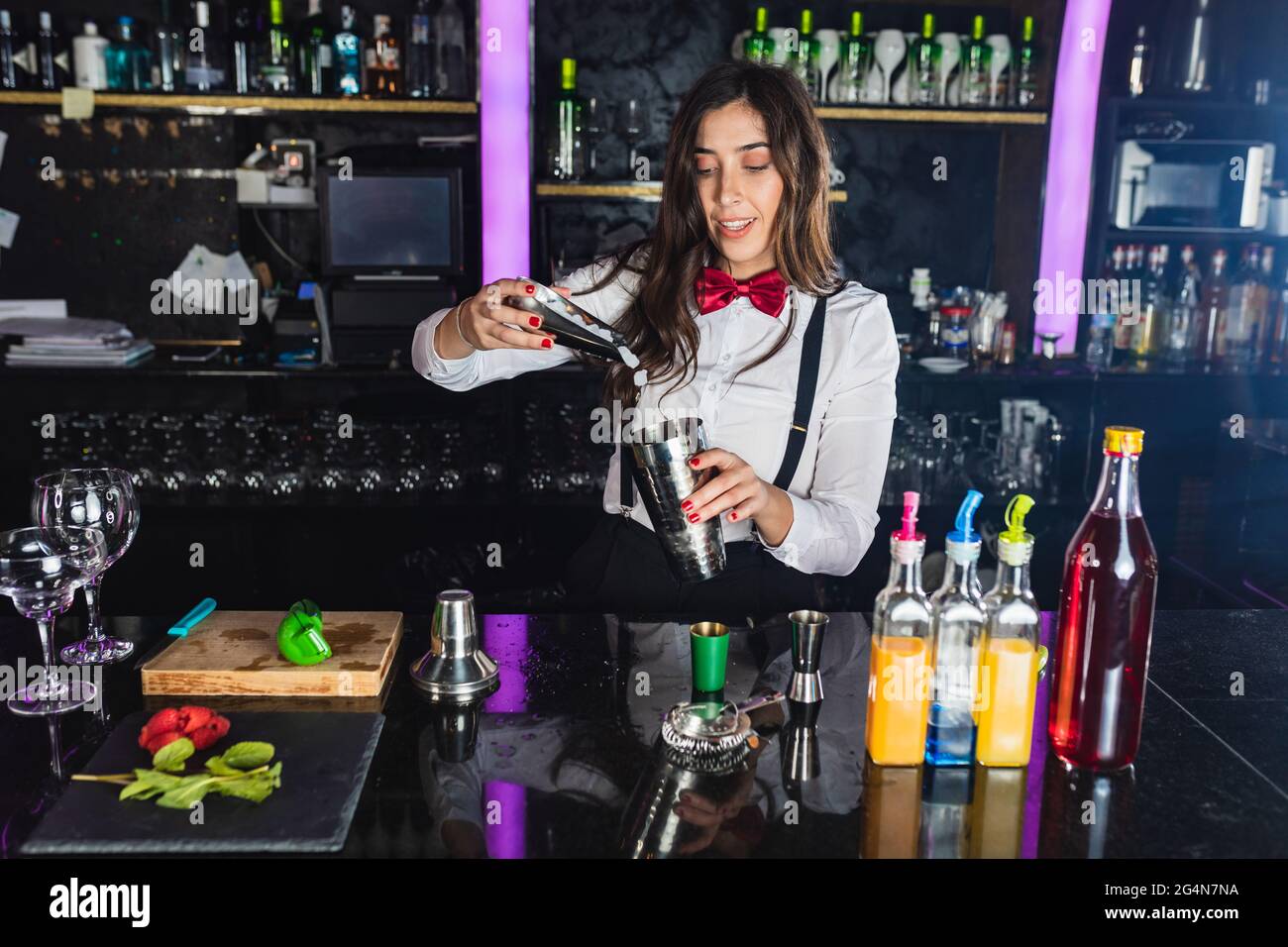 Female barkeeper in stylish outfit adding ice cubes into shaker while ...