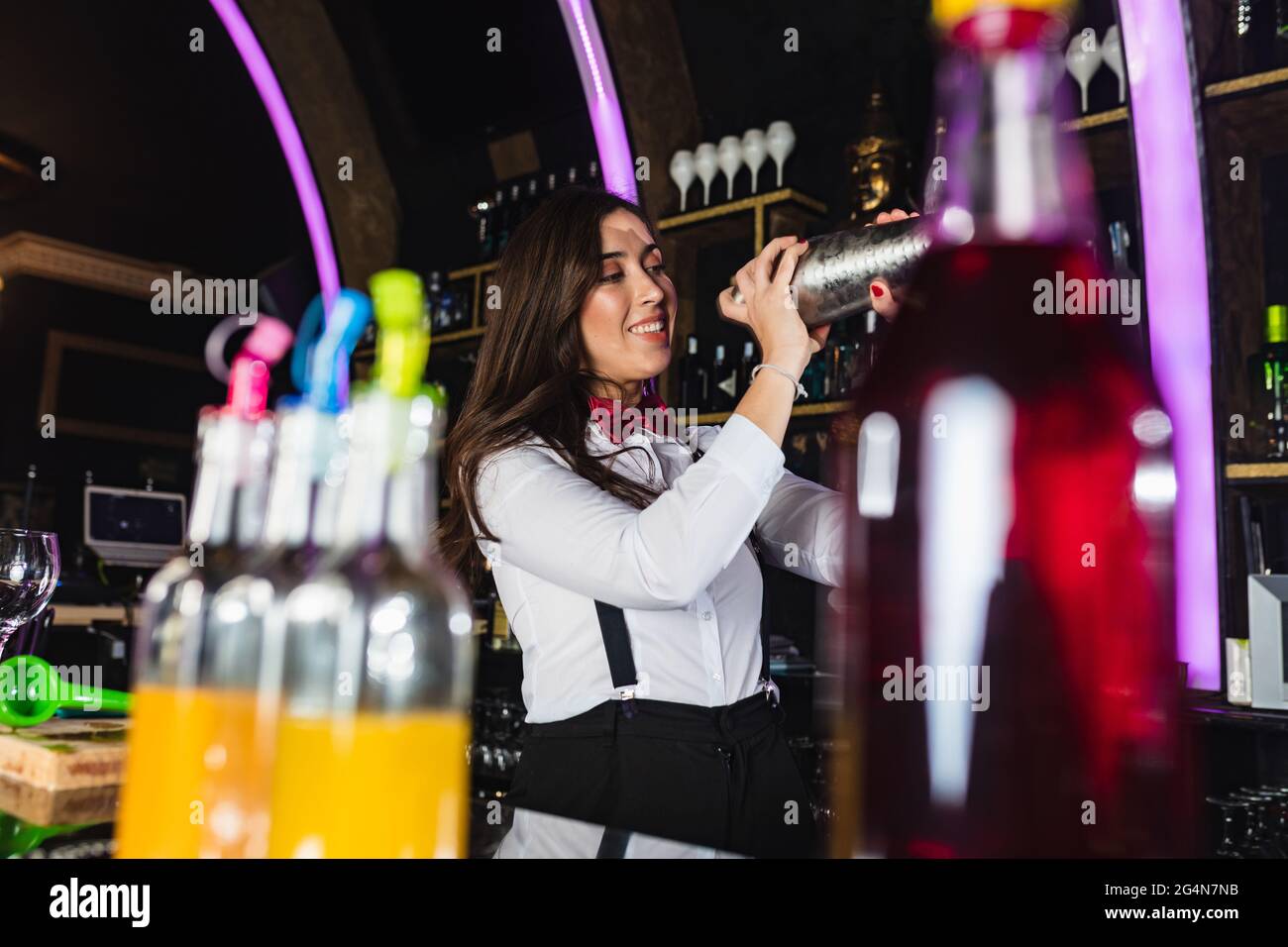 Happy female barkeeper in stylish outfit shaking metal shaker while ...