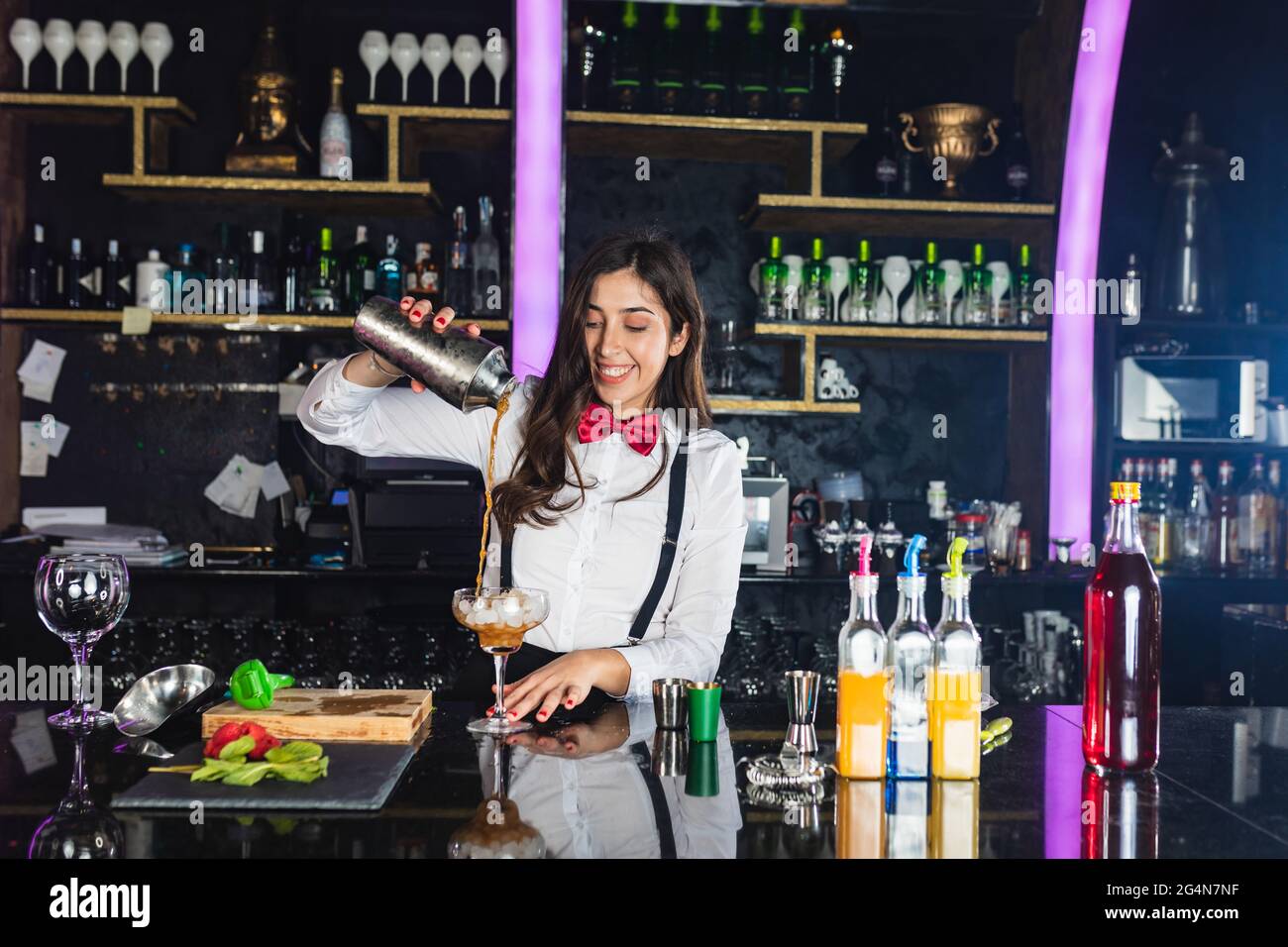 Smiling female barkeeper in stylish outfit serving cocktail from a ...